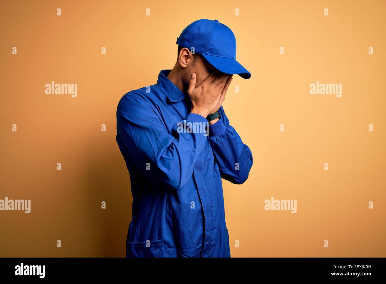 Young african american mechanic man wearing blue uniform and cap over ...