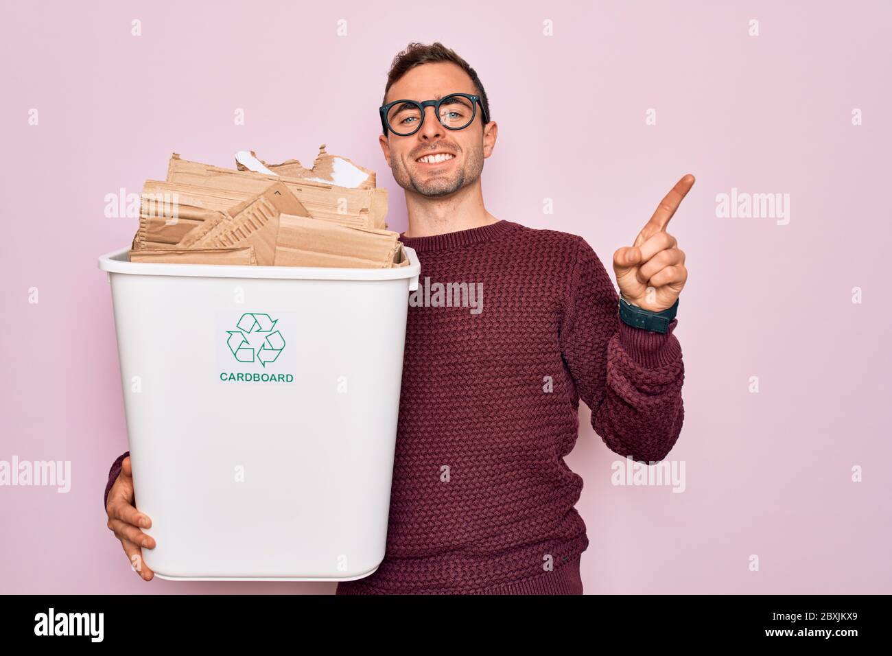Young handsome man with blue eyes recycling holding wastebasket with ...