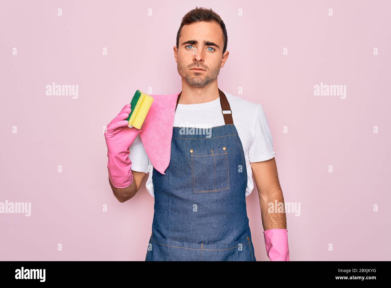 Young cleaner man with blue eyes cleaning wearing apron and gloves ...