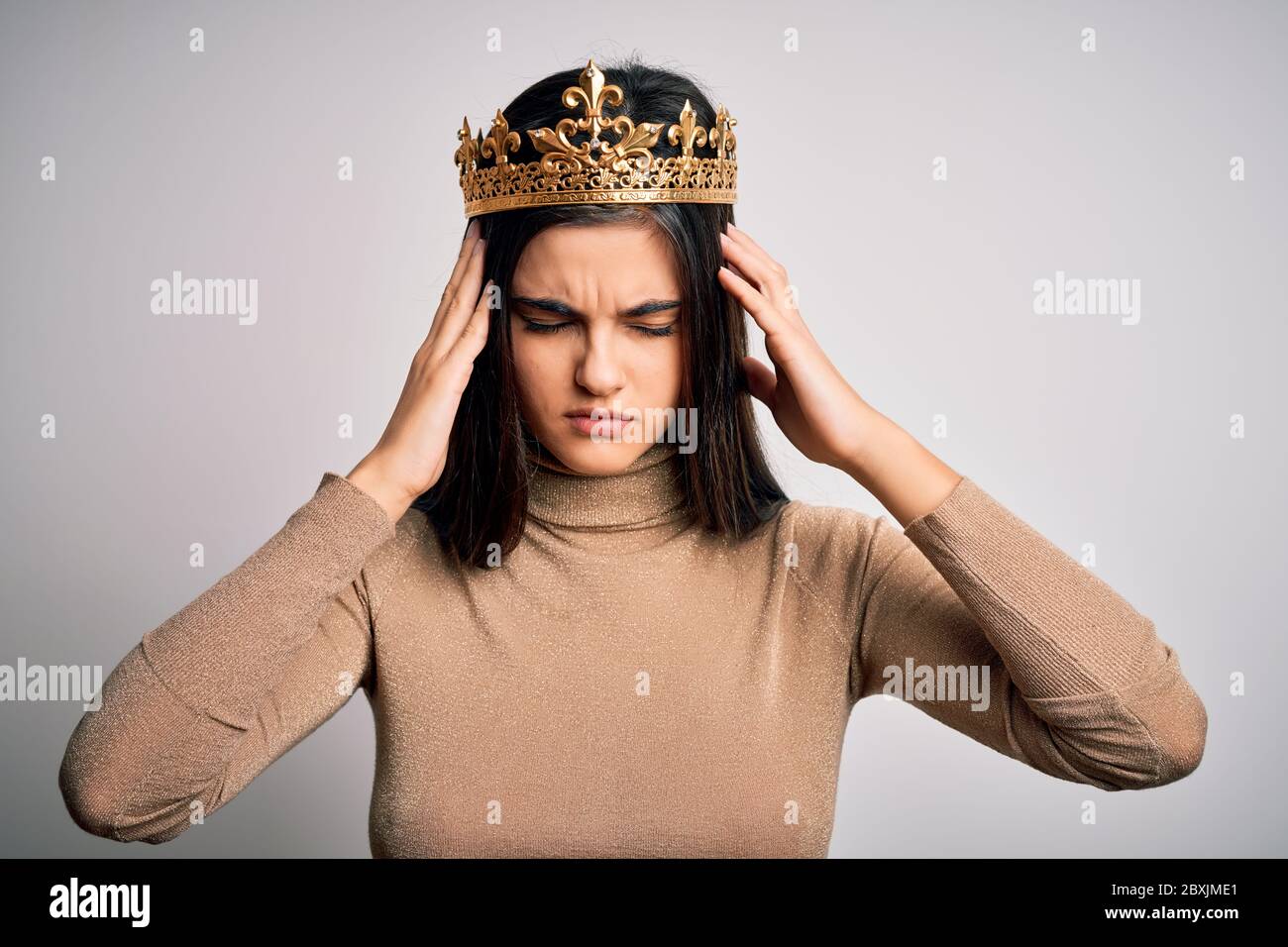 Young beautiful brunette woman wearing golden queen crown over isolated ...