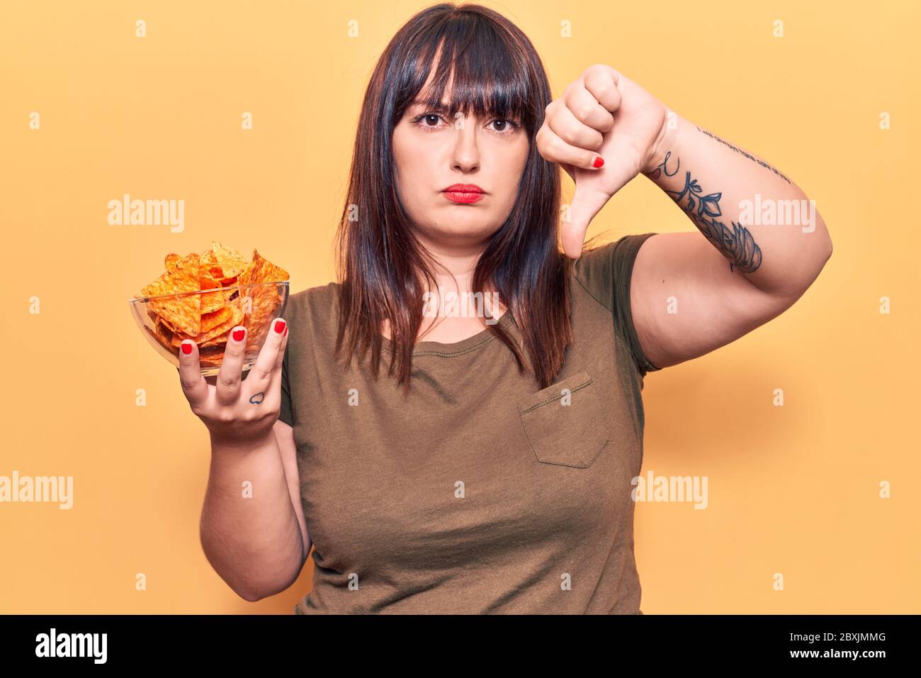 Young plus size woman holding nachos potato chips with angry face ...