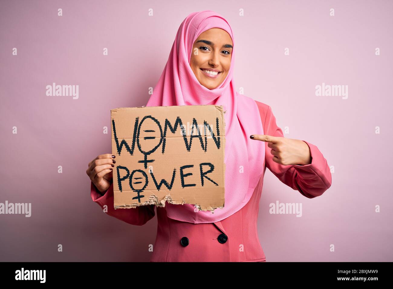 Young activist arab woman wearing pink muslim hijab holding banner with ...