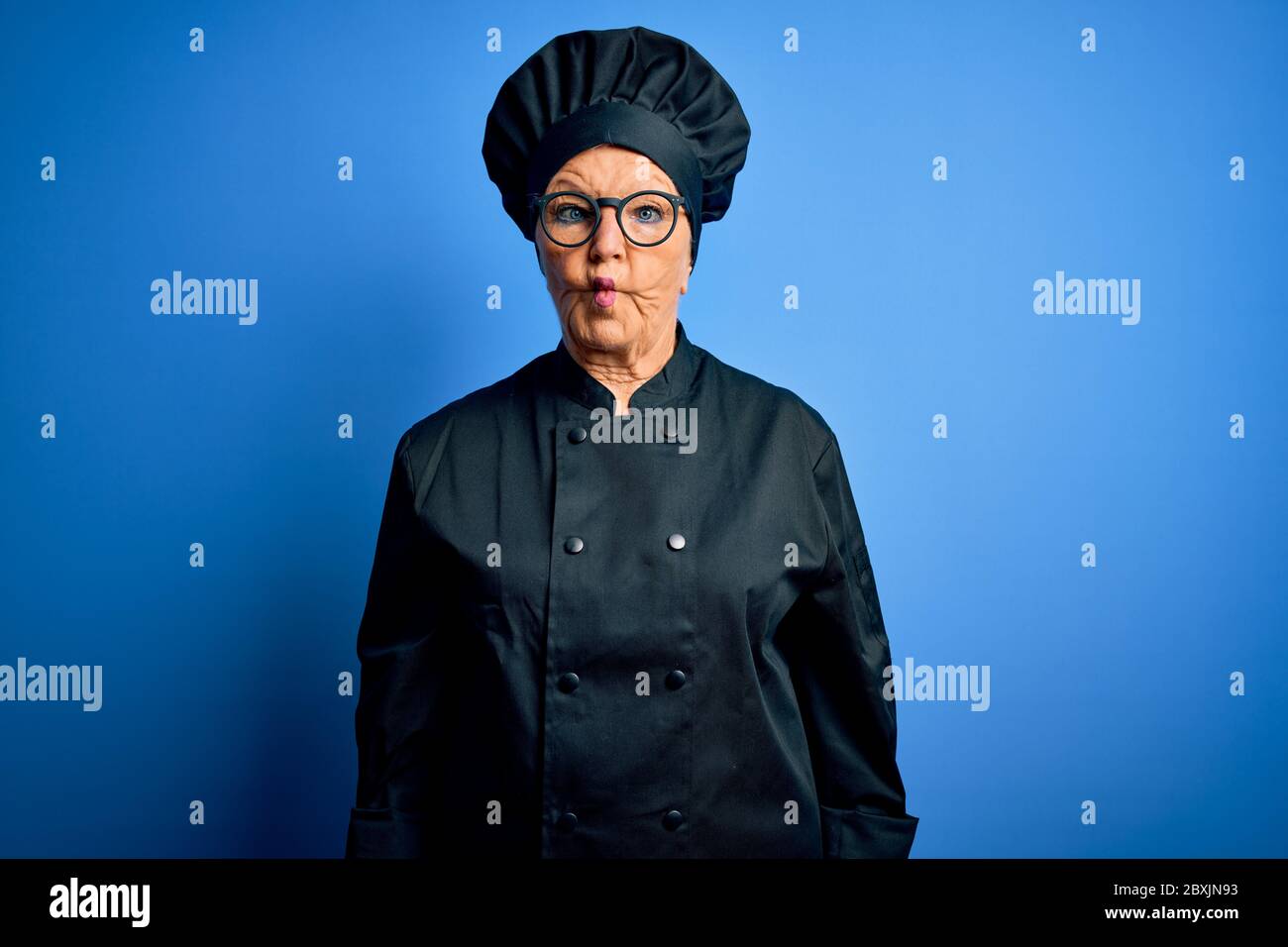 Senior beautiful grey-haired chef woman wearing cooker uniform and hat ...