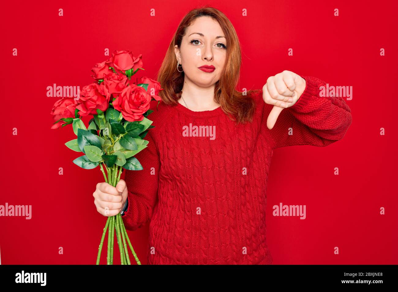 Young beautiful redhead woman holding bouquet of red roses flowers over ...
