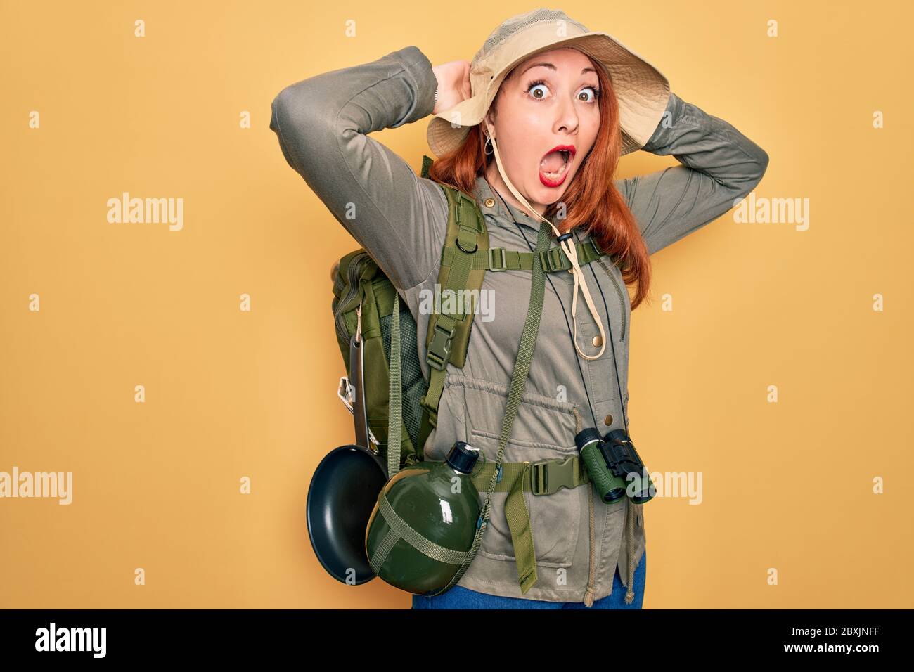 Young redhead backpacker woman hiking wearing backpack and hat over ...