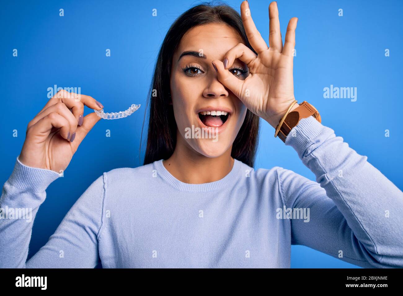 Young beautiful woman holding dental aligner to correction teeth over ...