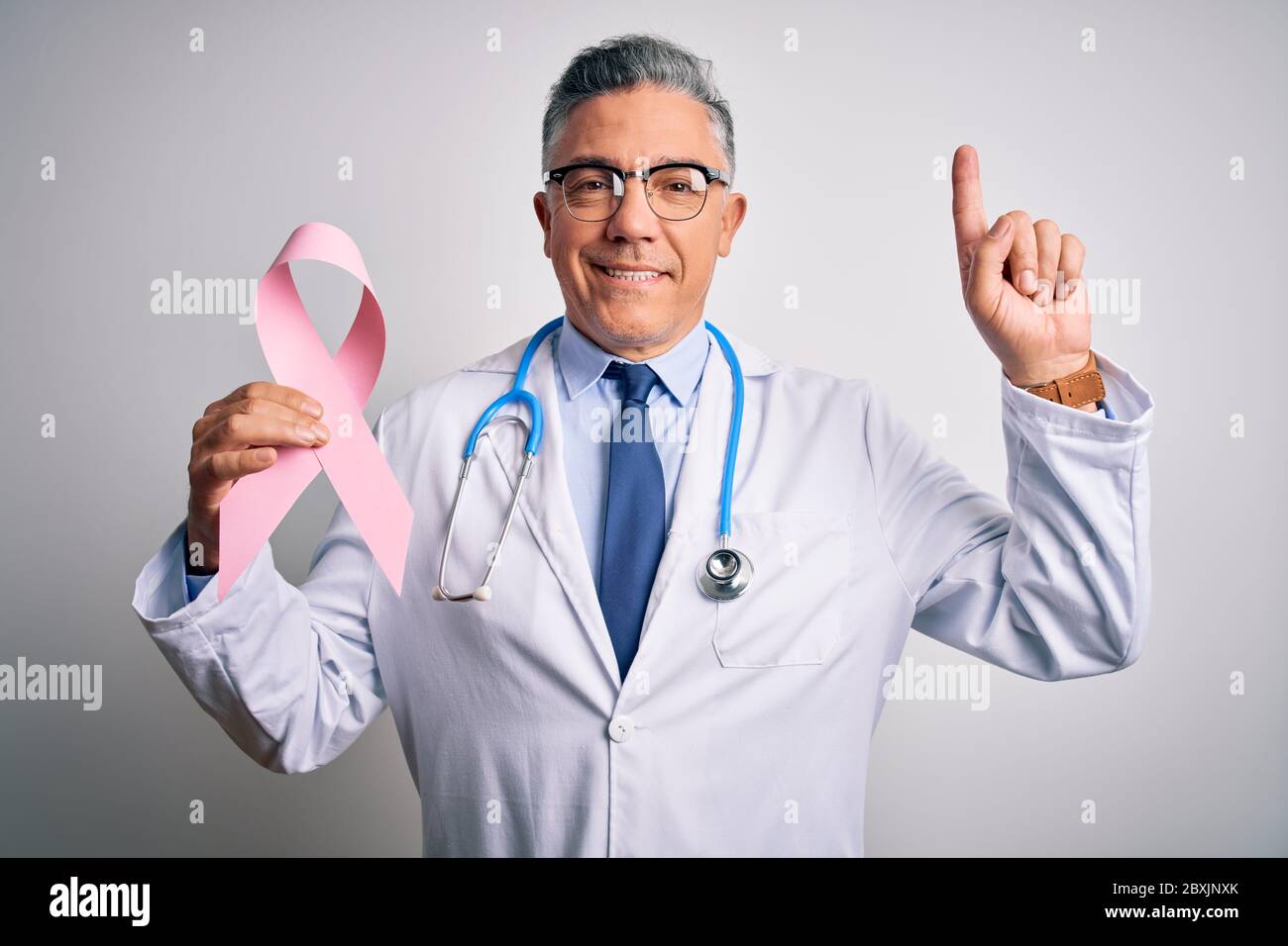 Middle age handsome grey-haired doctor man holding pink cancer ribbon ...