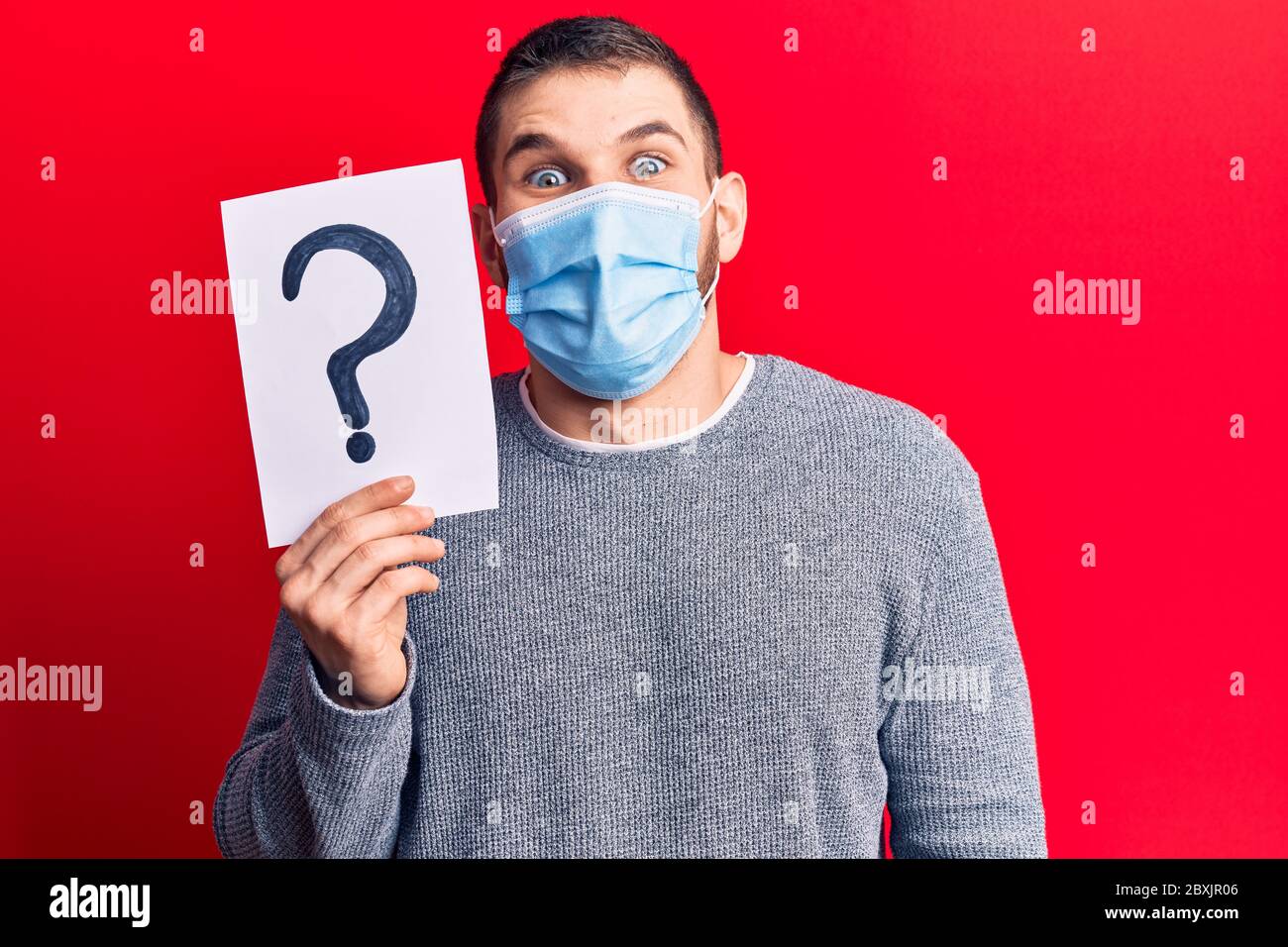Young handsome man wearing medical mask holding question mark scared ...