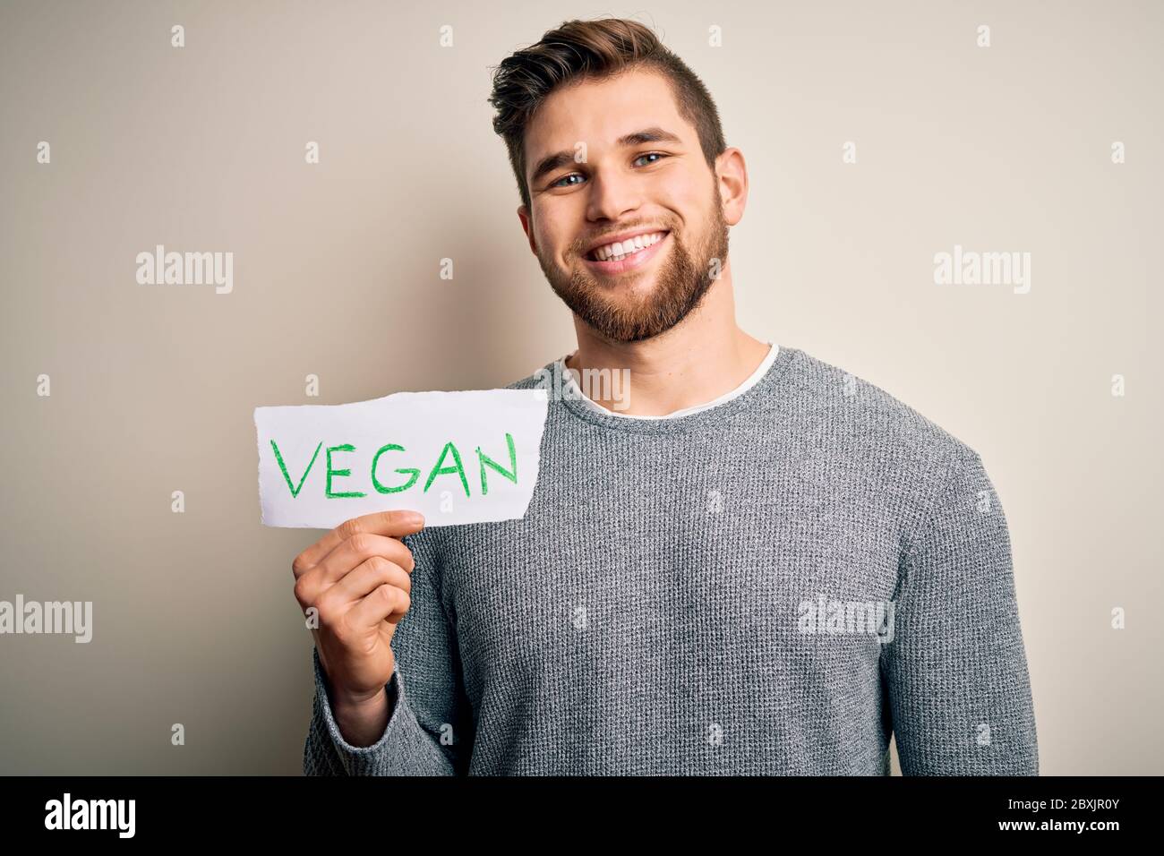 Young blond veggie man with beard and blue eyes holding paper with ...