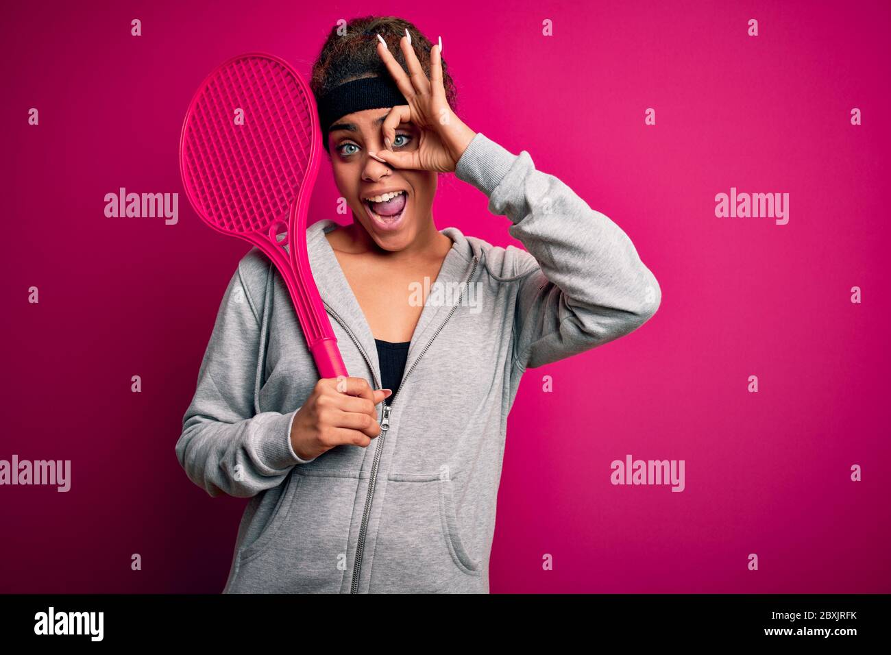 Young african american sportswoman playing tennis using racket over isolated pink background ...
