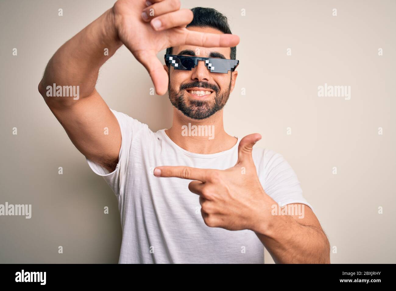 Young handsome man with beard wearing funny thug life sunglasses over ...