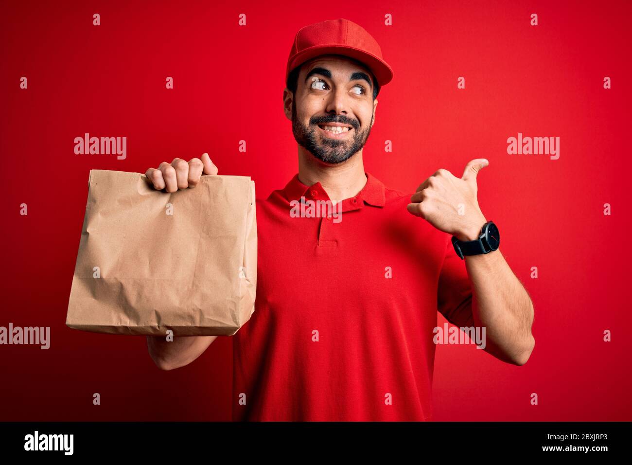 Young handsome delivery man with beard wearing cap holding takeaway ...
