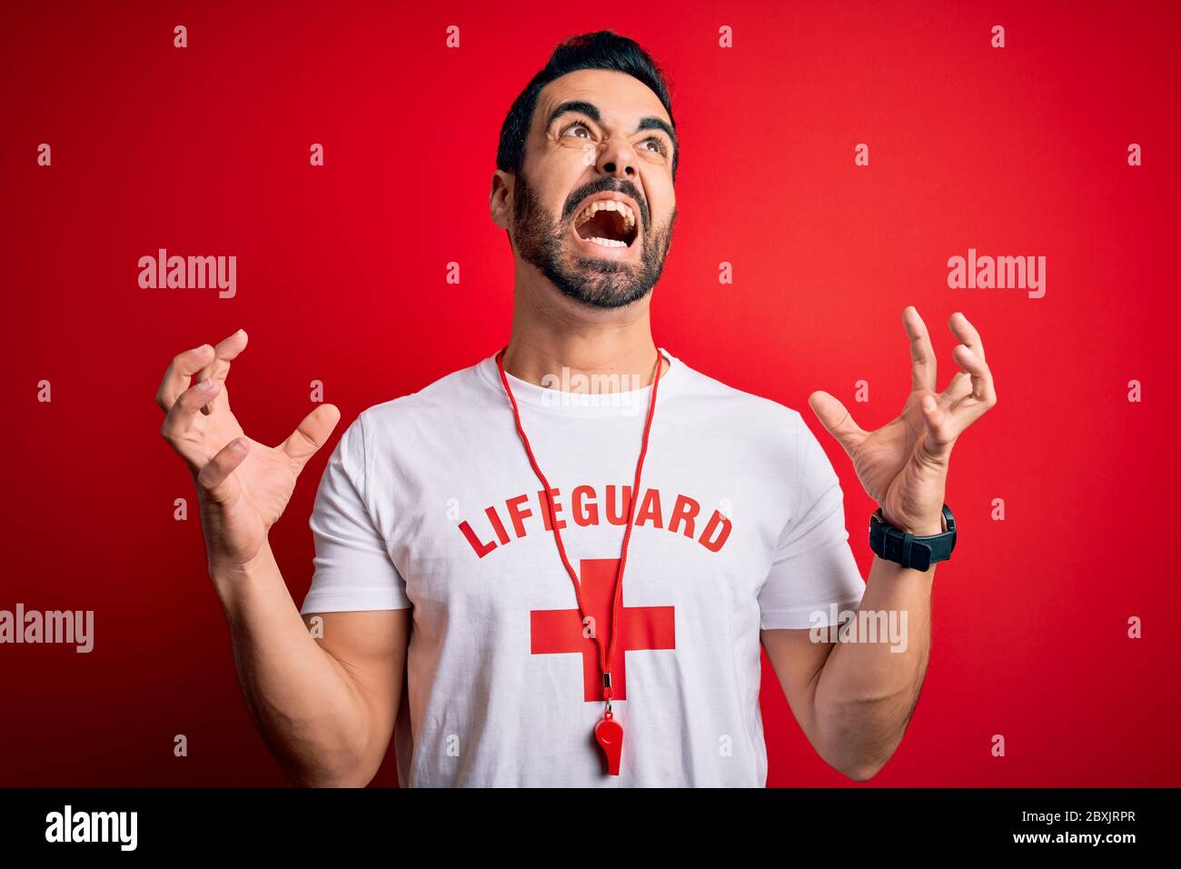 Young handsome lifeguard man with beard wearing whistle over isolated ...
