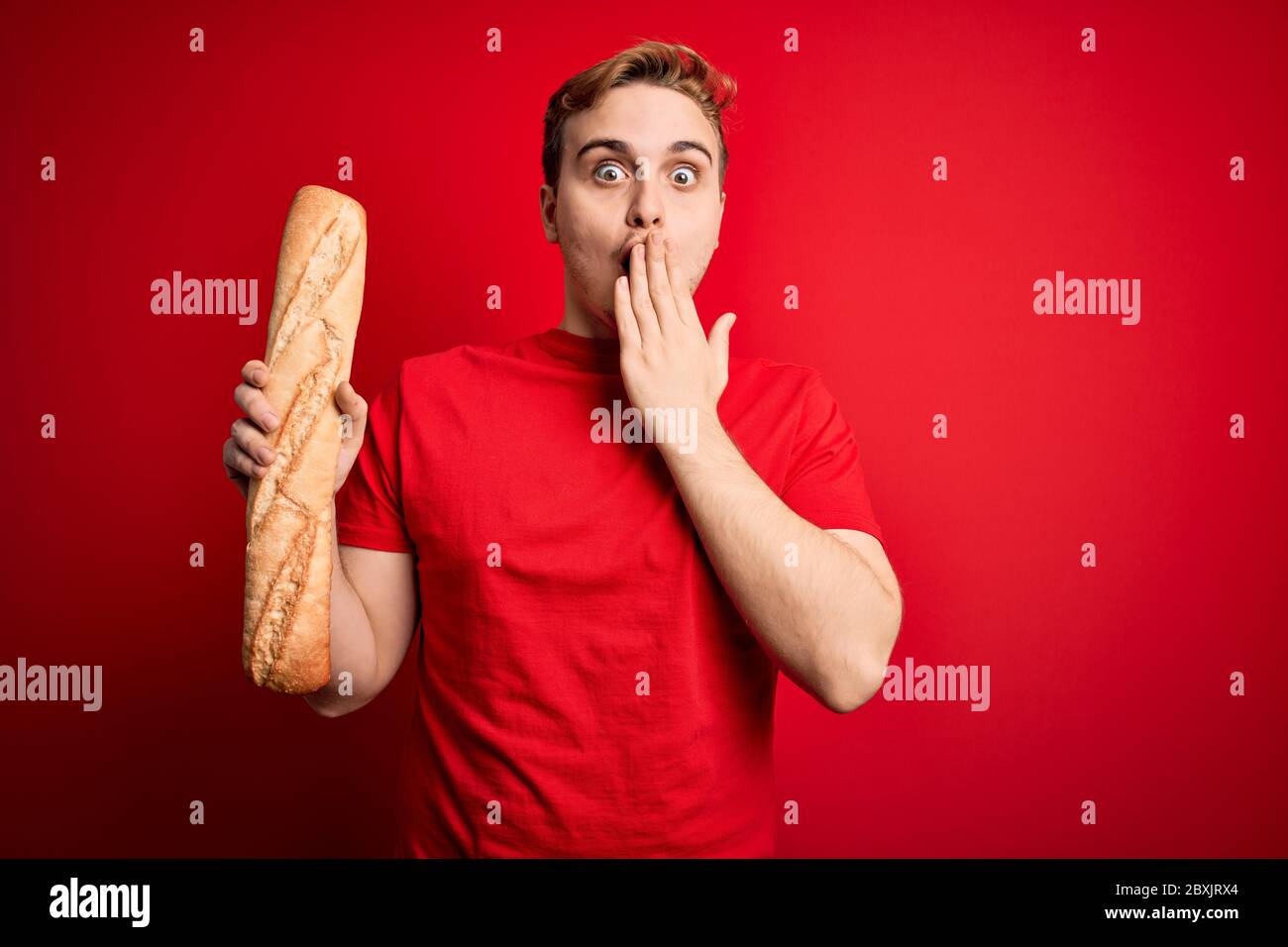 Young handsome redhead man holding fresh homemade bread over isolated ...