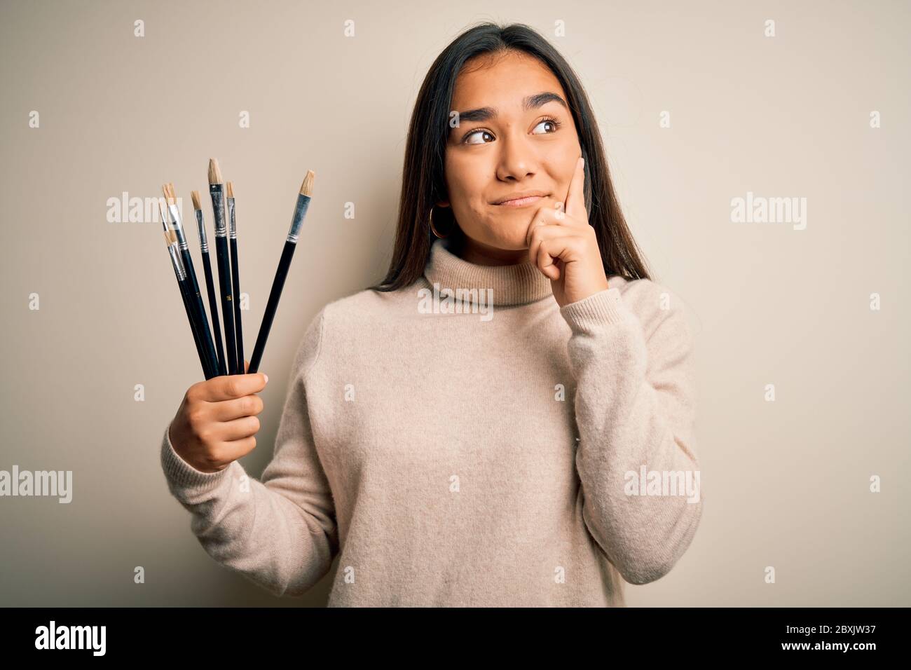 Young beautiful artist asian woman holding paint brushes standing over ...