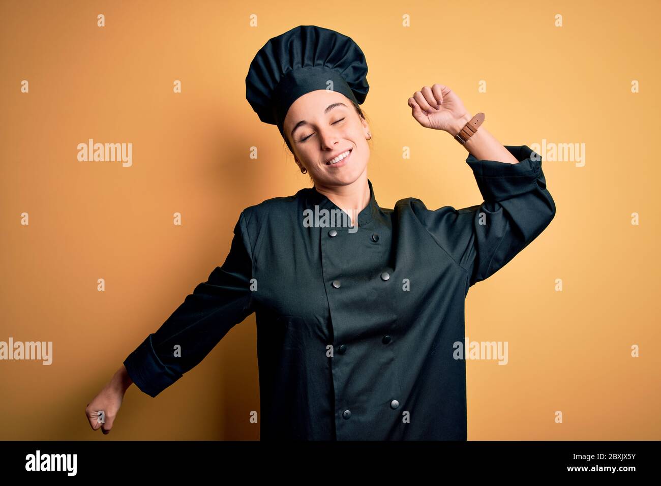 Young beautiful chef woman wearing cooker uniform and hat standing over ...