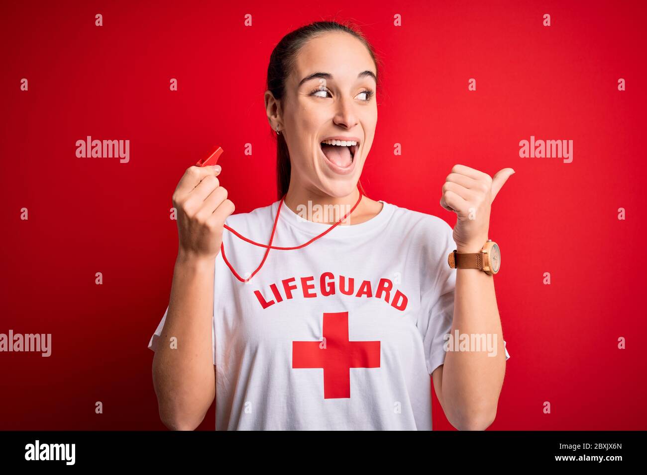 Beautiful lifeguard woman wearing t-shirt with red cross using whistle ...