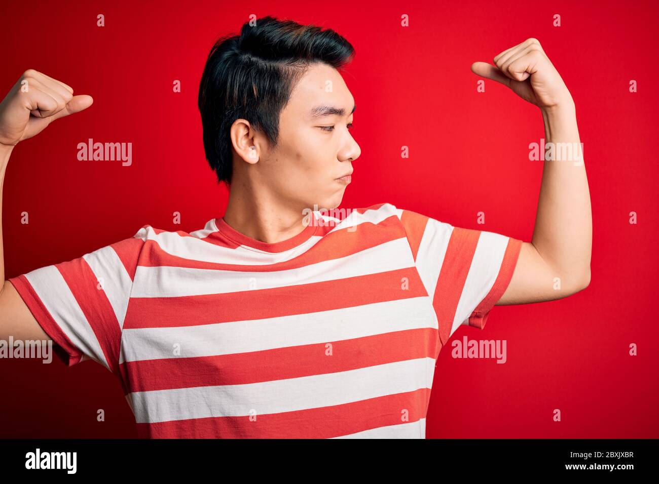 Young handsome chinese man wearing casual striped t-shirt standing over ...