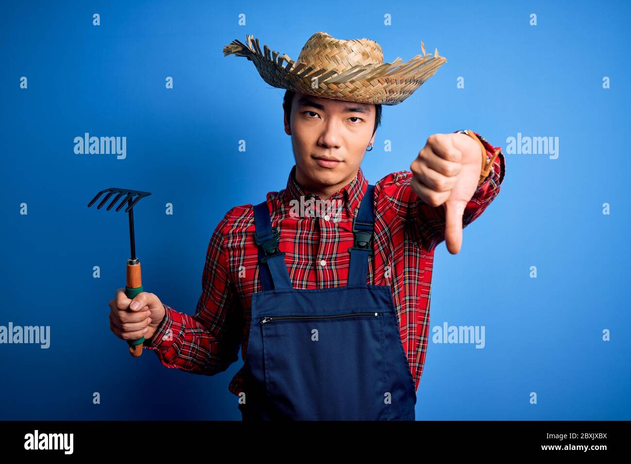 Young handsome chinese farmer man wearing apron and straw hat holding ...