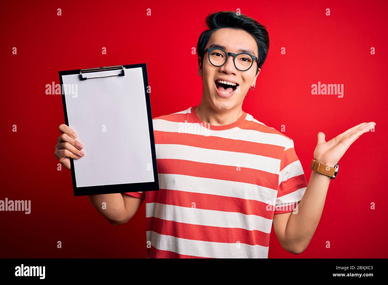Young handsome chinese inspector man wearing glasses holding clipboard ...