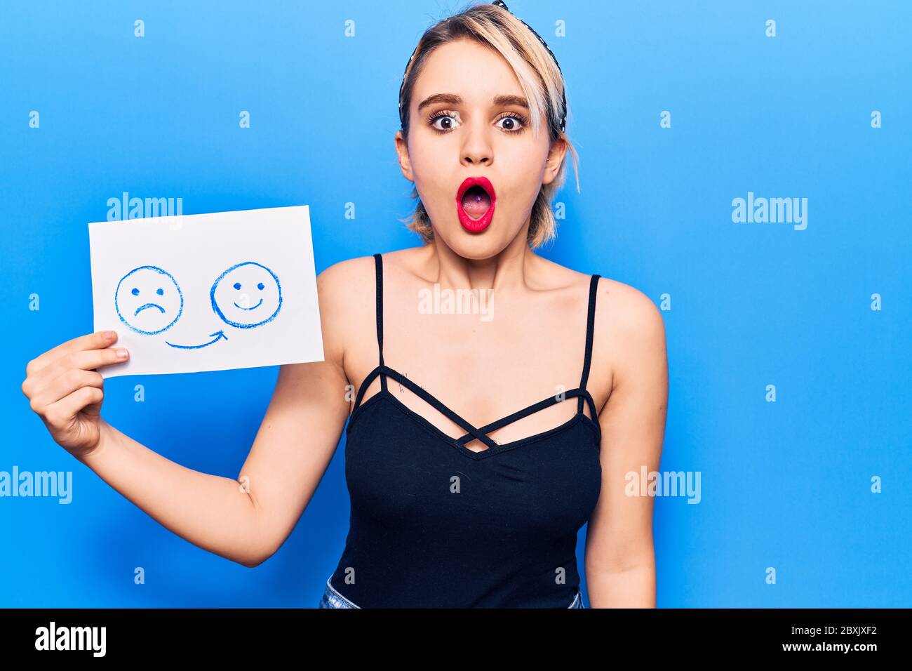 Young beautiful blonde woman holding sad to happy emotion paper scared ...