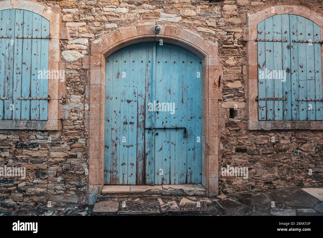Closed blue wooden door and windows in old stone brick Cyprus building ...