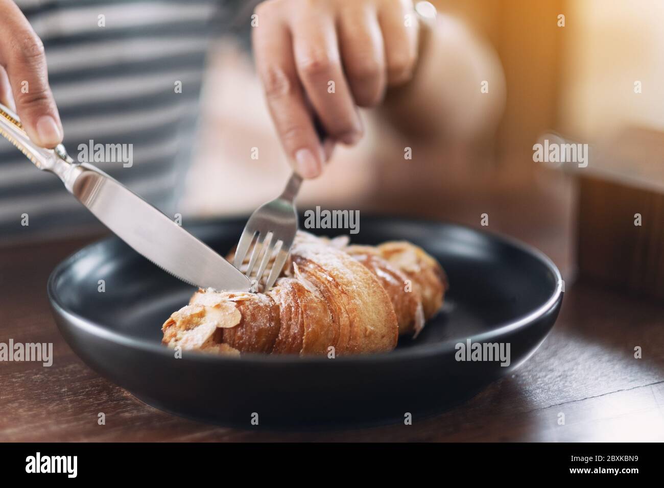 Closeup image of a woman eating a piece of croissant by knife and fork ...