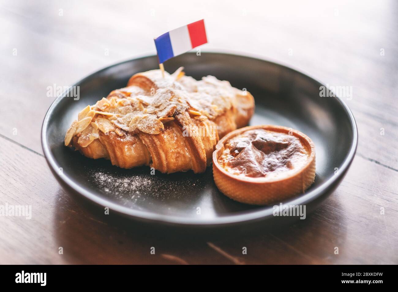 A piece of croissant and tart with a flag of France in a black plate on ...