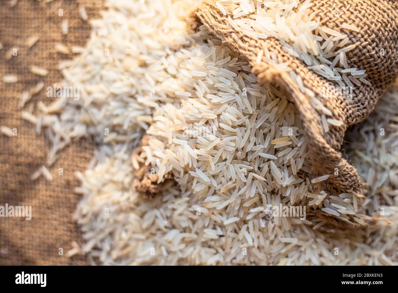 Close up shot of Raw Basmati white rice in a gunny bag on brown surface ...