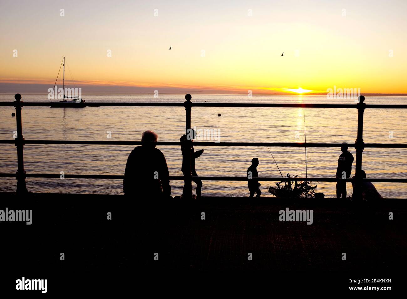 Beachfront scene at sunset people in silhouette fishing rods snugging ...