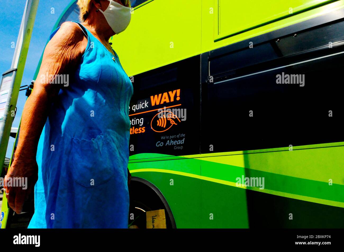 Retired older lady woman wearing covid19 mask face covering at bus stop ...