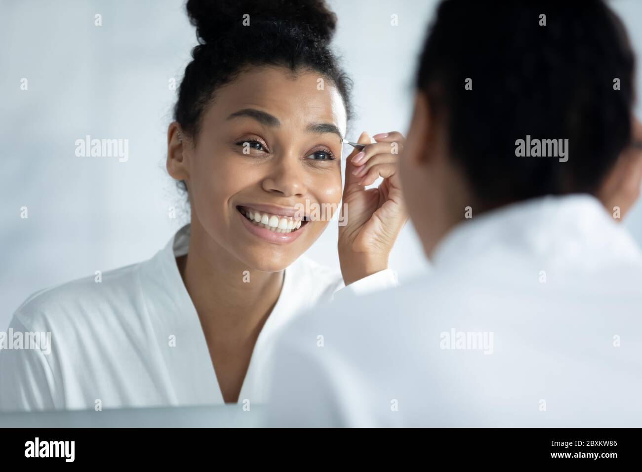 Mirror reflection smiling African American woman plucking eyebrows with ...