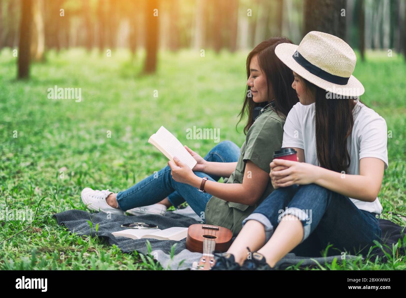 Two women reading book together while sitting in the woods Stock Photo ...