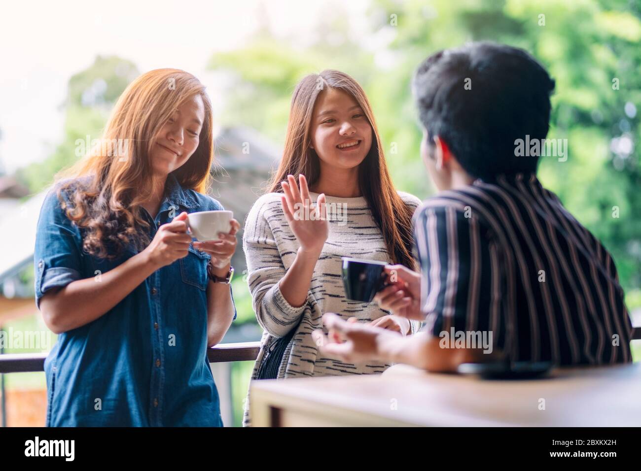 A woman greeting and say hi to her male friends while drinking coffee ...