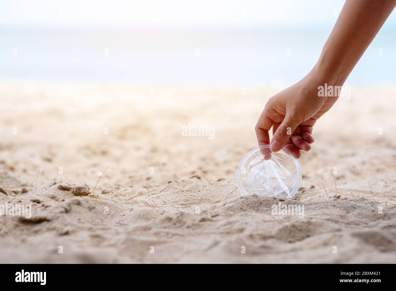 A hand cleaning and picking up a plastic glass trash on the beach Stock ...