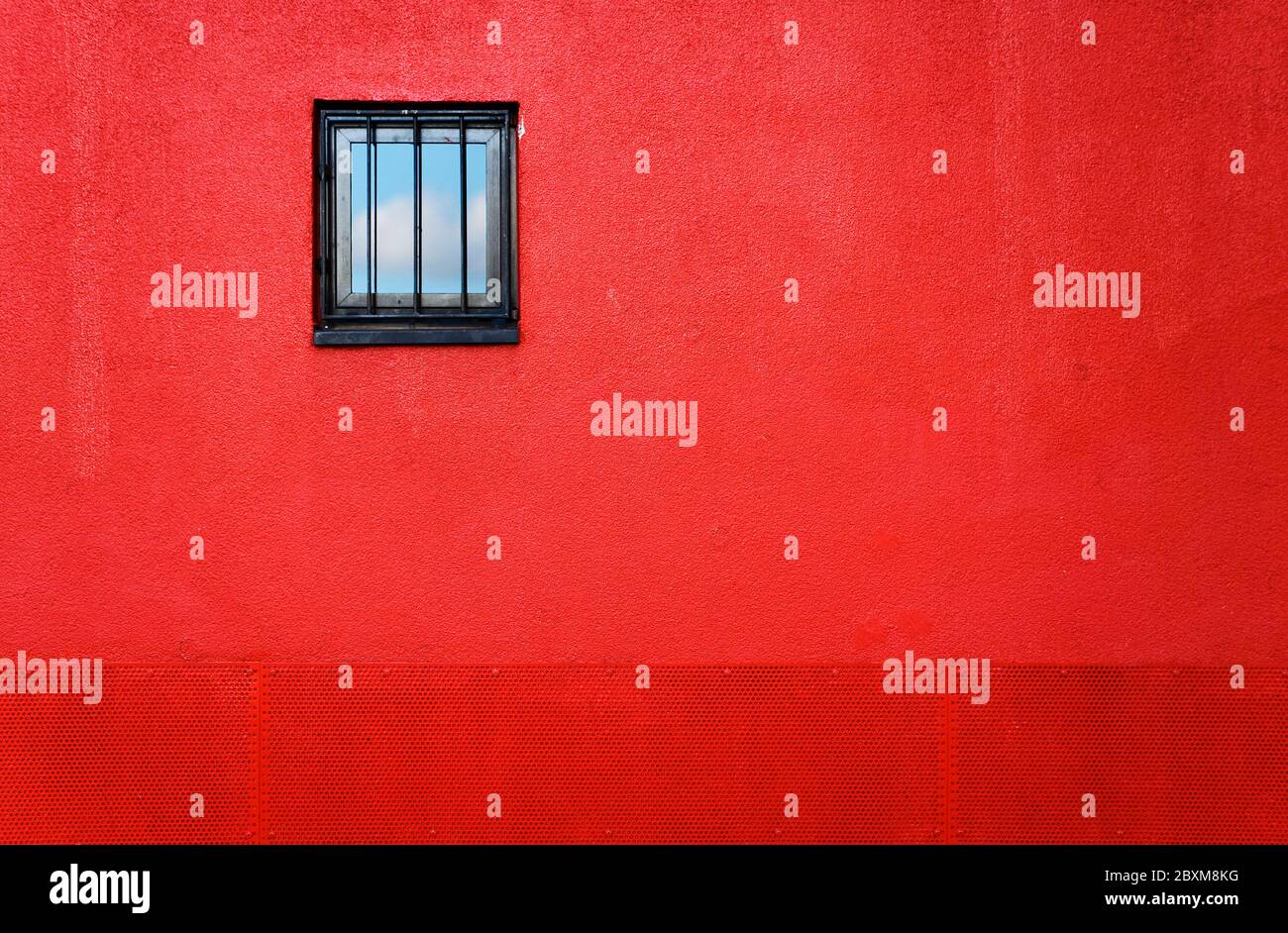 red painted wall with small barred window, sky reflected within Stock ...