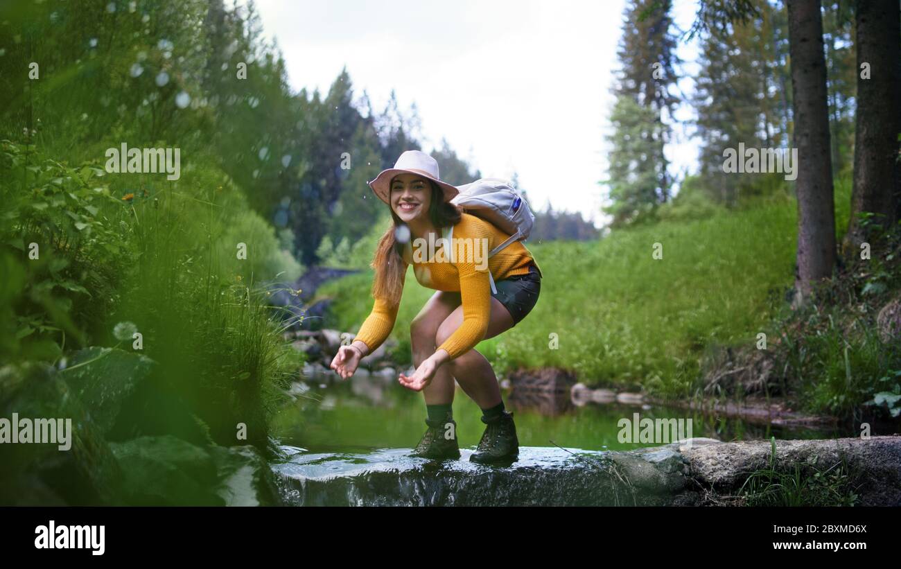 Happy young woman standing by stream on a walk outdoors in summer ...