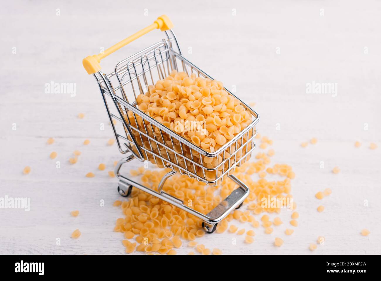 Close up photo of small shopping trolley with pasta over white wooden ...