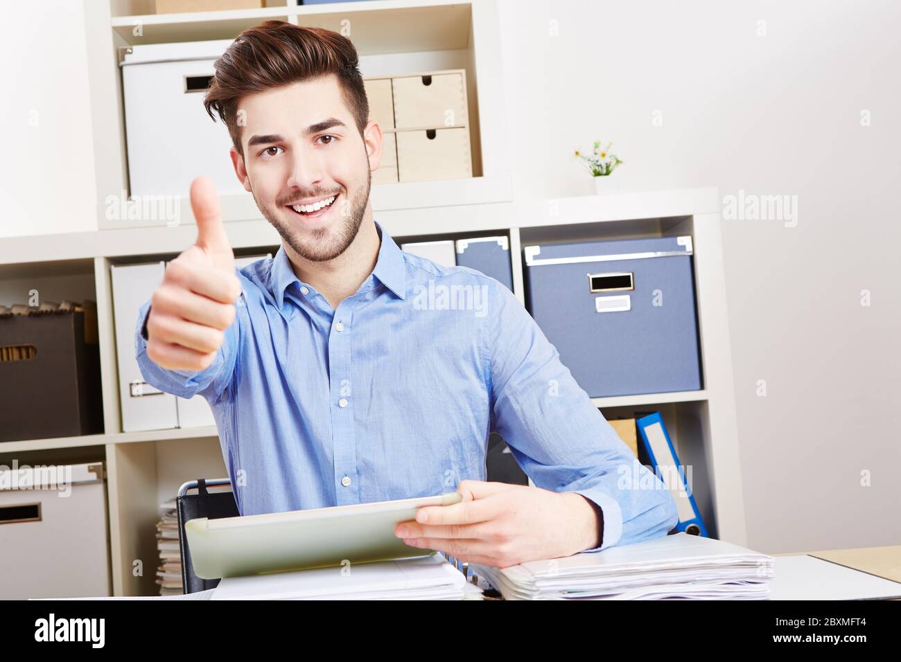 Laughing man with tablet computer in the office holds his thumb up ...