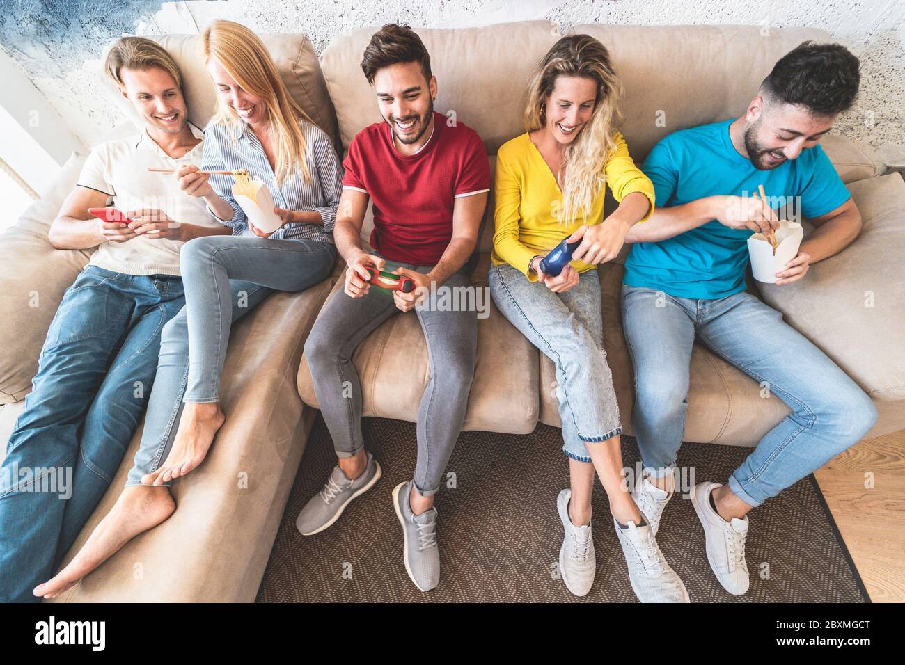 Young people playing console game while eating delivery asian food at ...