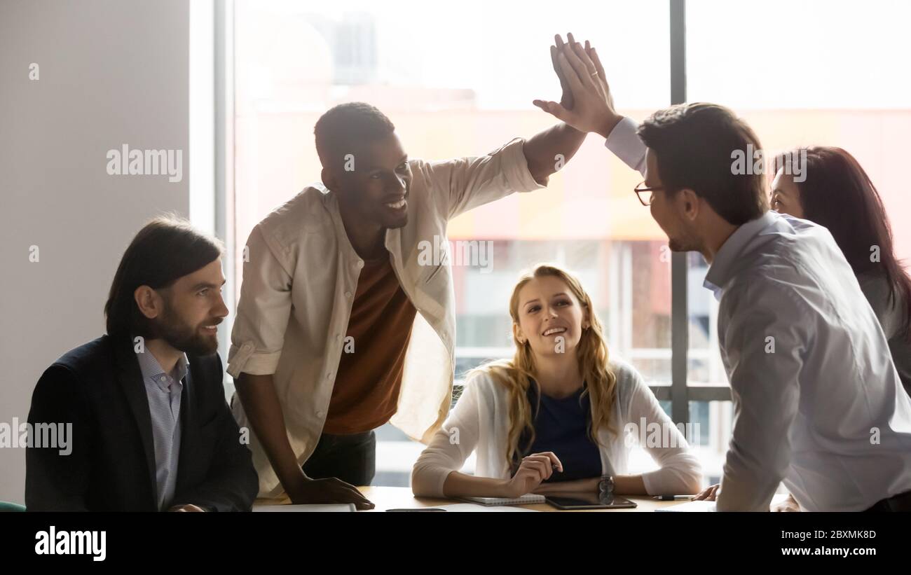Multiethnic teammates giving high five sharing success during group ...