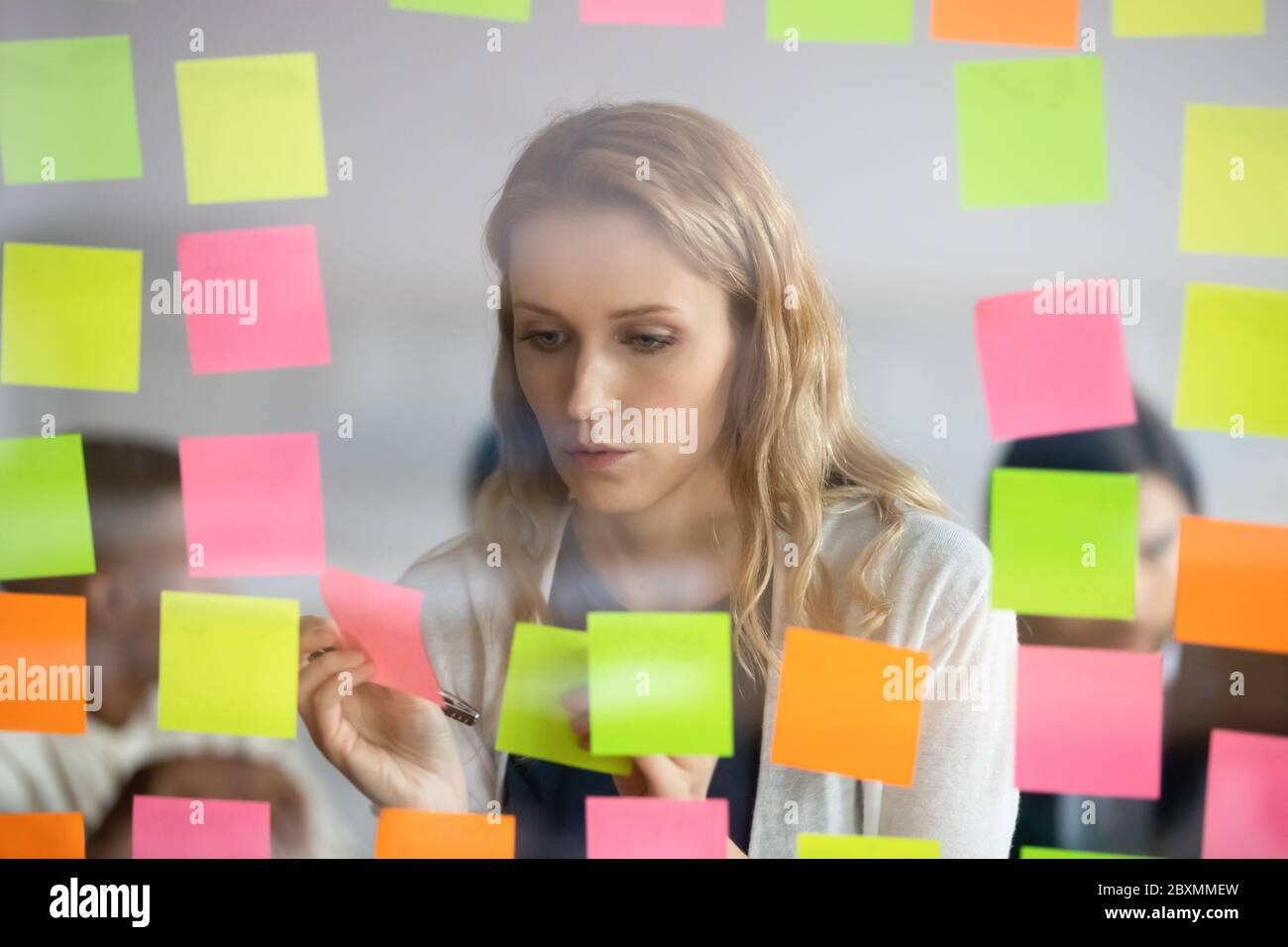 Businesswoman attaching to wall colorful sticky notes with tasks Stock ...