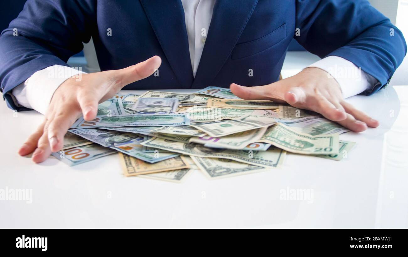 Greedy rich businessman grabbing heap of money from his desk. Concept ...