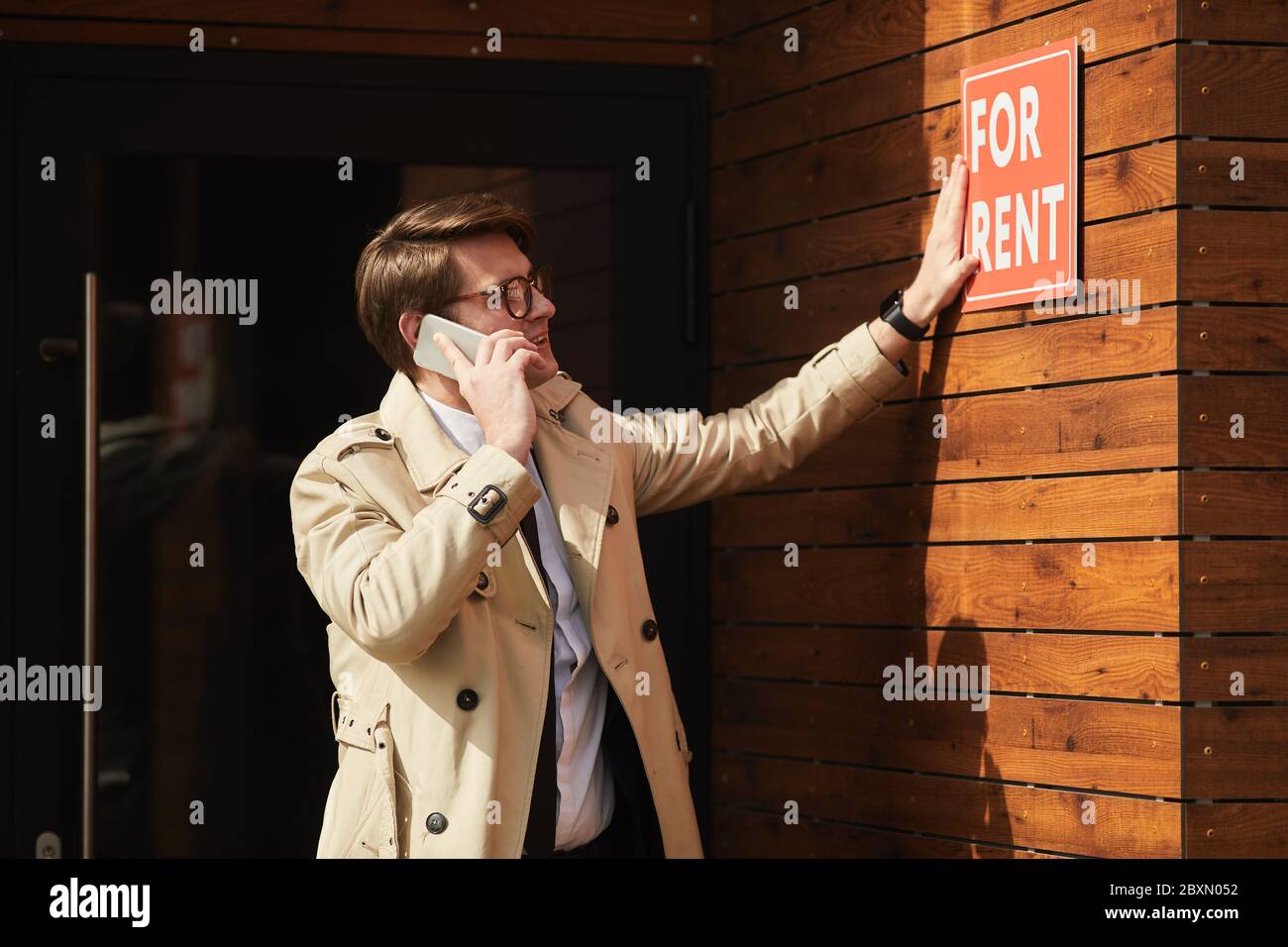 Waist up portrait of male rental agent hanging FOR RENT sign on office ...