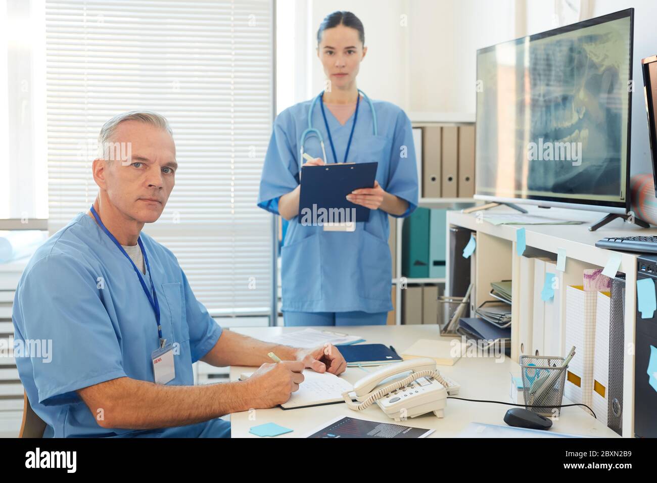 Portrait of two adult doctors wearing blue uniforms looking at camera ...