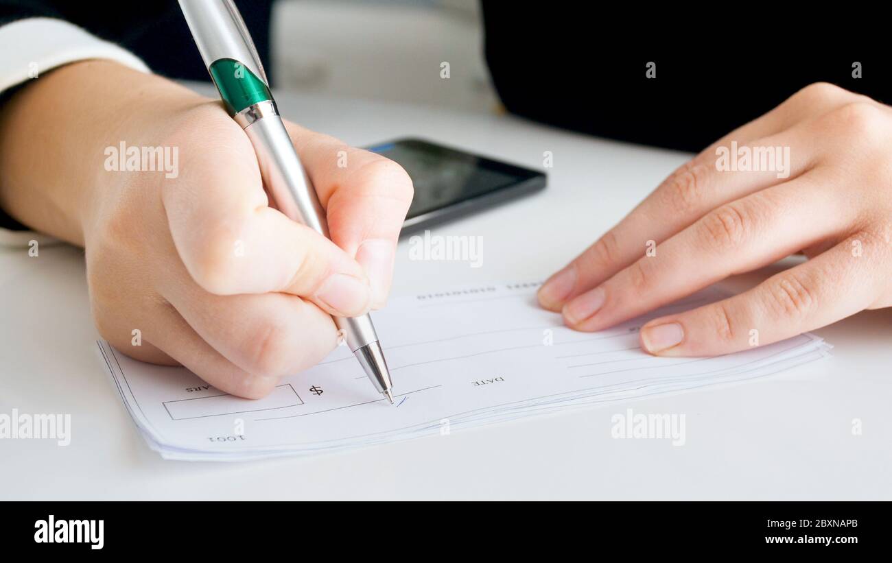 Closeup image of woman writing signature on banking cheque Stock Photo ...