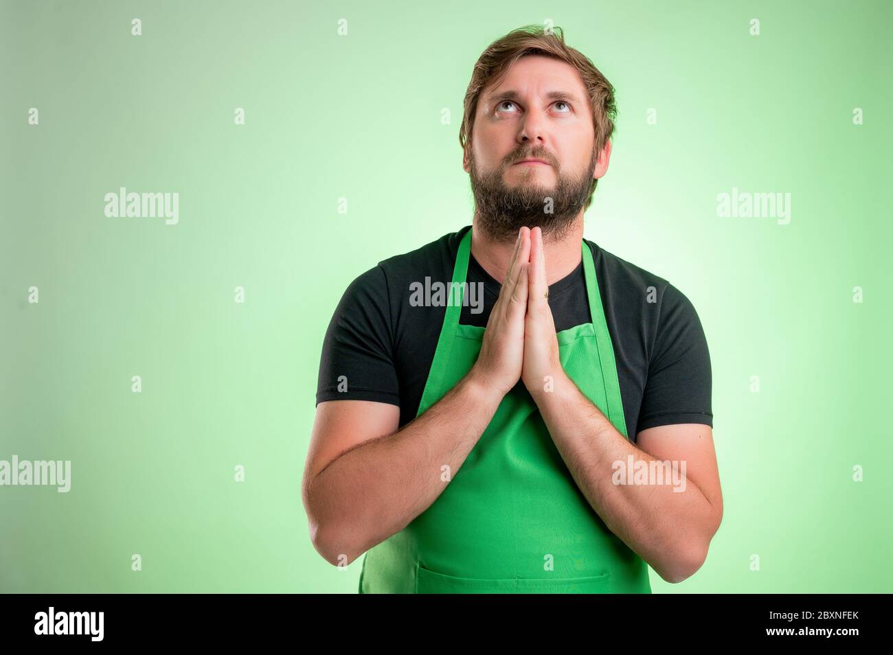 Supermarket employee with green apron and black t-shirt, praying ...