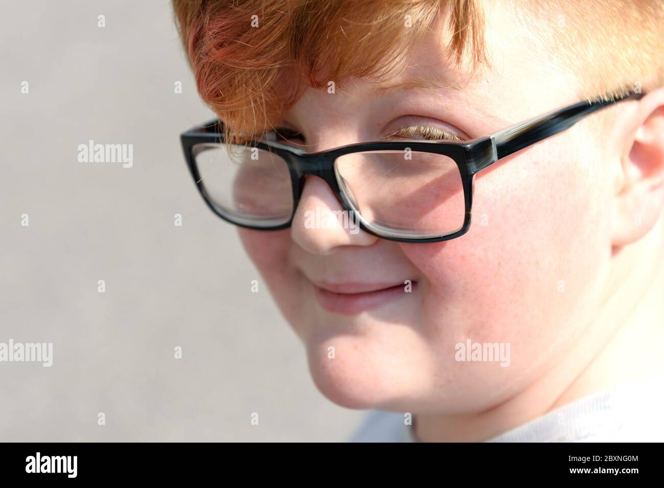 Portrait of a cute red-haired boy wearing glasses smiling and looking ...