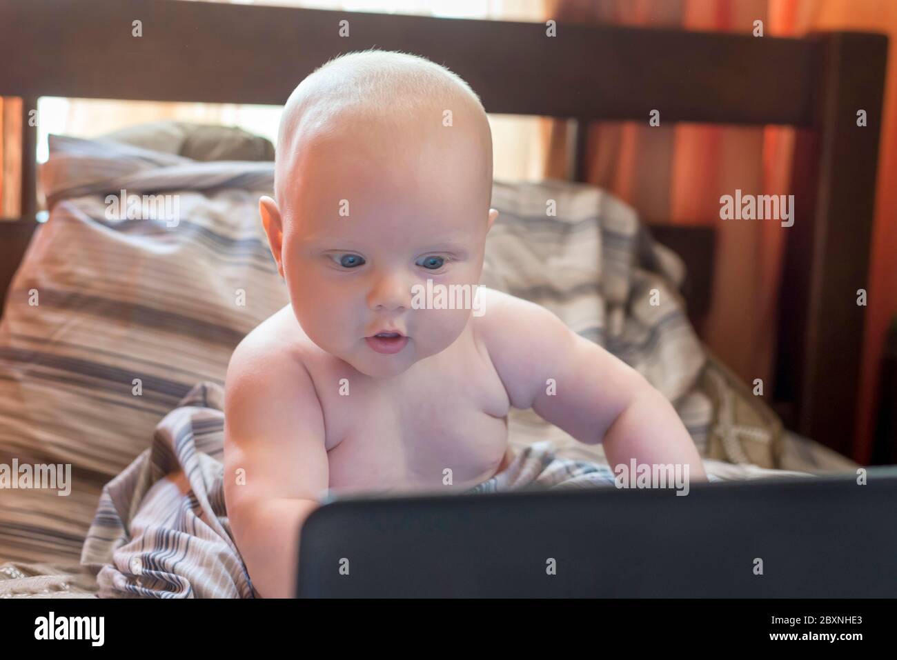 Little cute surprised baby sitting in front of laptop in bed Stock ...