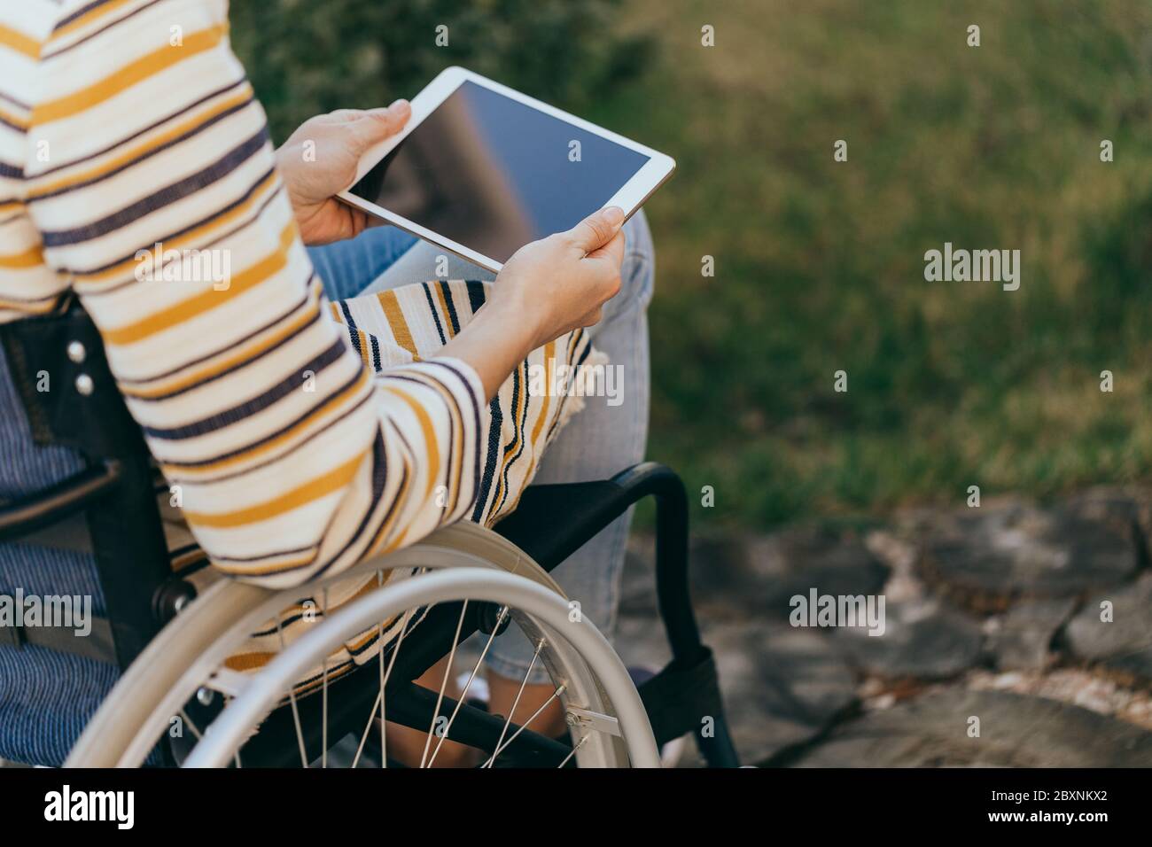 Fashionably dressed woman in a wheelchair with a modern tablet in hand ...